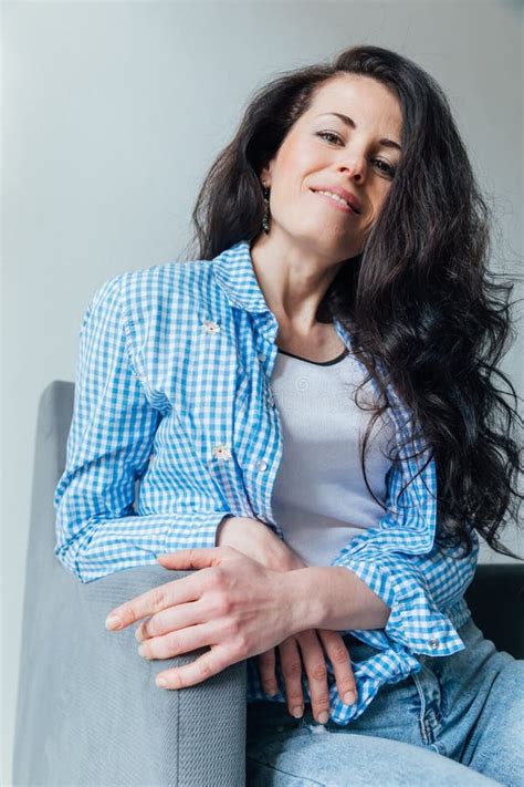 A Brunette Woman In Denim Sitting In A Chair In A Room Stock Image
