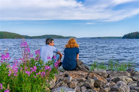 화창한 여름 저녁에 호수 베이의 해안에 돌에 앉아 관광객 검은 머리 남자와 빨간 머리 젊은 여자 사람들은 휴식과 라도가 호수의 아름다운 풍경을 존경 카렐리아 러시아 2명에