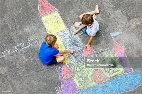 아스팔트에 화려한 분필로 기사 성을 그리는 두 어린 아이 소년 행복한 형제 자매와 친구들은 분필 그림과 그림을 만드는 재미를