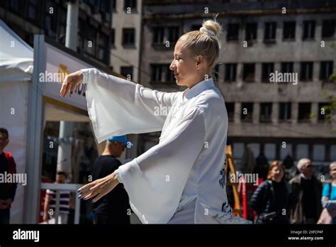 A Serene Tai Chi Master In A Flowing White Suit Gracefully Performs On A Bustling Street Her