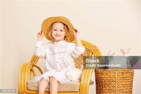 고리버들 모자를 쓴 하얀 벽에 맞서 집에서 고리버들 의자에 앉아 있는 하얀 토끼가 귀엽고 행복해하는 소녀 아이 2 3 살에 대한 스톡 사진 및 기타 이미지 Istock