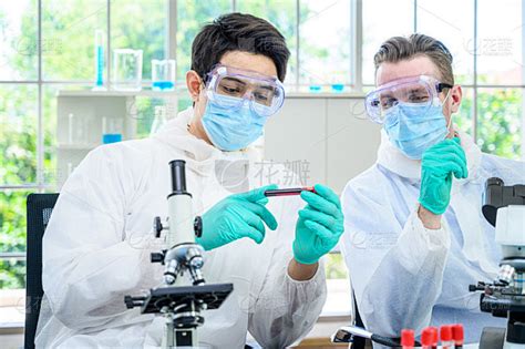 一对男科学家穿着防护服，拿着疫苗，在实验室里用许多实验室设备研究疫苗。