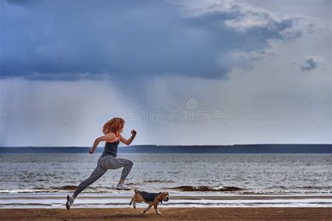 A Red Haired Middle Aged Woman In Sportswear Runs Along The Sandy Shore