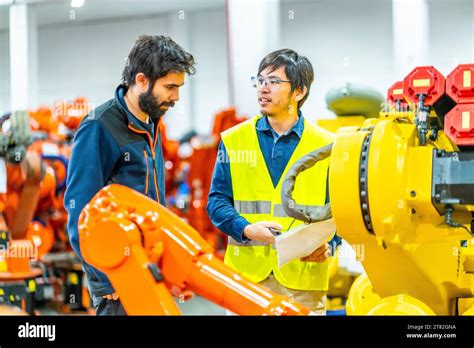 Japanese And Caucasian Engineers Controlling The Production Of Industrial Robotic Arms Stock