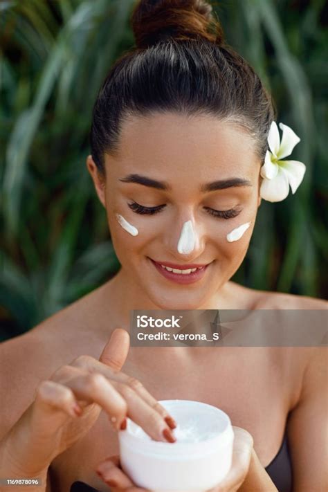 뷰티 우먼 컨셉 스킨 케어 화장품 크림을 들고 부드러운 피부와 젊은 모델 열대 자연에서 보습 크림과 터치 자신의 얼굴을 적용 여성의 초상화 건강관리와 의술에 대한 스톡 사진