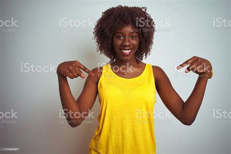 고립된 흰색 배경 위에 노란색 티셔츠를 입은 젊은 아프리카 아프로 여성은 얼굴에 미소를 지으며 자랑스럽고 행복한 손가락으로 자신을 가리킵니다 T 셔츠에 대한 스톡 사진 및