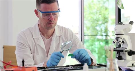 engineer looks at microcircuit through magnifying glass in workshop