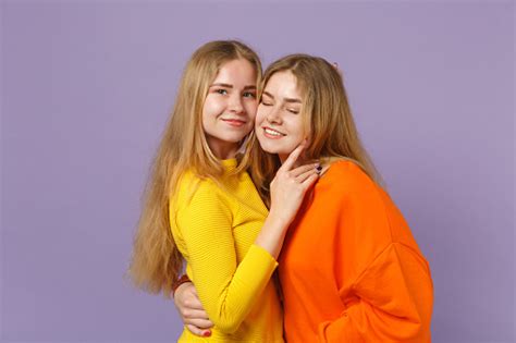 두 웃는 젊은 금발 쌍둥이 자매는 생생한 다채로운 옷에 여자를 포옹 하 고 찾고 파스텔 바이올렛 블루 벽 배경에 고립 된 카메라 사람들 가족 라이프 스타일 개념입니다 복사