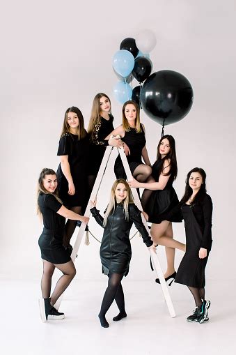 밝은 방에서 생일을 축하하는 재미가 검은 드레스에 행복한 젊은 일곱 여자 화려한 공기 풍선으로 장식 사다리에 포즈를 취하는