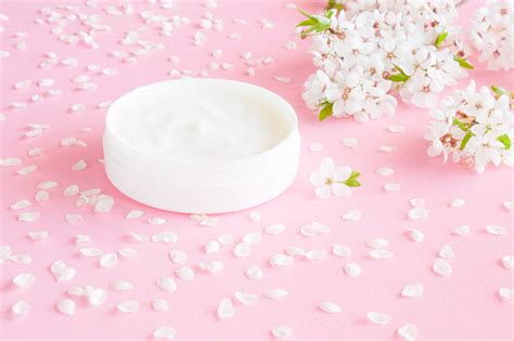 파스텔 핑크 바탕에 여성을 위한 천연 허브 크림의 흰색 병 열 꽃잎과 벚꽃의 아름 다운 분기 합니다 깨끗 하 고 부드러운 얼굴 손 다리와 바디 피부에 관심이 있다 신선한