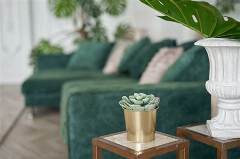 전경에 있는 하우스플랜트 쿠션 에메랄드 색 소파 쪽모이 세공 마룻바닥 벽난로 소파 및 하우스 플랜트가있는 고급 거실 벽에 치장