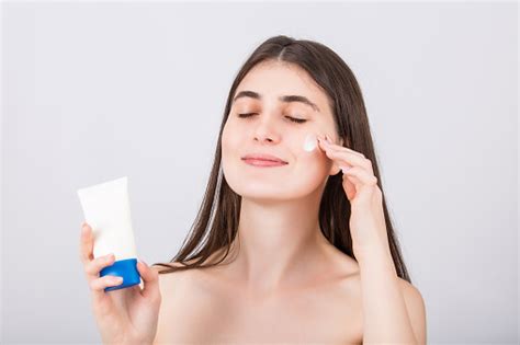 연화 얼굴 크림을 바르는 아름다운 여자는 흰색 배경에 격리된 보습 화장품이 든 튜브를 손에 들고 있다 스킨케어 개념 및