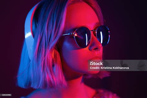 염색 된 머리와 선글라스와 화려한 아가씨는 헤드폰에서 음악을 듣고 네온 빛 배경으로 노래 눈을 감고 춤을 추는 매력적인 힙스터