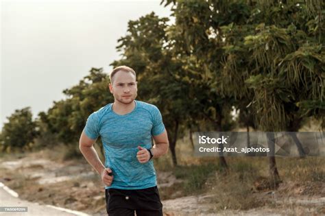 푸른 티셔츠와 검은 반바지를 입은 백인 남자의 초상화가 일몰 동안 아스팔트 트랙에서 훈련하고 달리는 T 셔츠에 대한 스톡 사진 및 기타 이미지 Istock