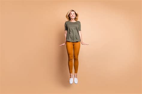 미친 여자 점프 높은 흥분 여름 분위기 현대 모습 수줍은 사람 착용 녹색 T 셔츠 노란색 바지 운동화 고립 된 베이지 색 배경의 전체 길이 사진 T 셔츠에 대한 스톡 사진