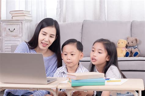 집에서 두 아이의 숙제를 가르치는 아시아 싱글맘 홈스쿨 학습 라이프스타일 사용 현대 기술 노트북 또는 수업 시청 교사와 온라인 참여 멀티태스킹 모성 30 34세에 대한 스톡
