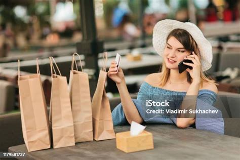 온라인 쇼핑 전화로 이야기하고 그녀의 손에 은행 카드를 들고있는 동안 야외 카페에 앉아 쾌활한 젊은 쇼핑 중독자 여자 가방에 대한 스톡 사진 및 기타 이미지 Istock