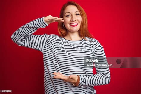 크고 큰 크기의 간판을 보여주는 손으로 빨간 고립 된 배경 몸짓 에 서 있는 끈 을 입고 있는 젊은 빨간 머리 여자 기호를 측정 합니다 카메라를 바라보며 웃고 있습니다 측정