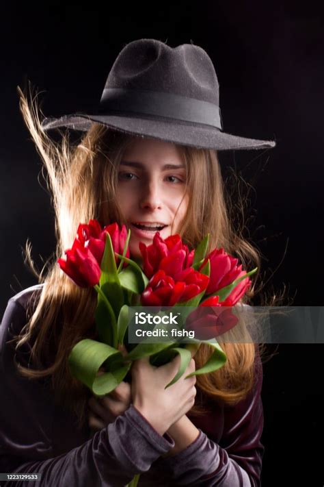 보라색 드레스를 입은 소녀와 어두운 배경에 챙이 넓은 검은 모자를 쓴 소녀는 빨간 튤립 꽃을 손에 들고 버드 아이와 함께 닫습니다 갈색 머리에 대한 스톡 사진 및 기타