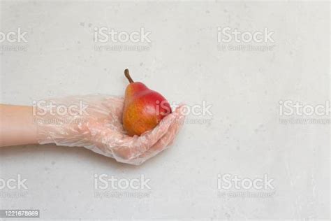 일회용 투명 장갑에 손레드 배 과일을 보유 빨간 배는 밝은 회색 흰색 현대 콘크리트 배경에 일회용 투명 장갑에 손에 놓여있습니다