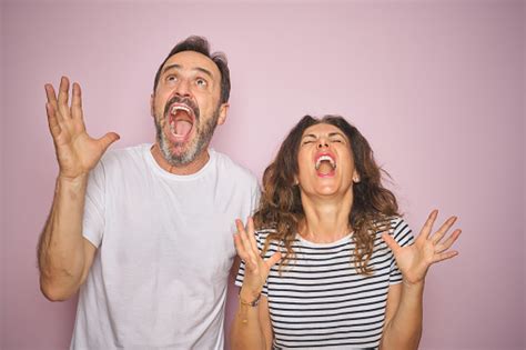아름다운 중년 부부는 함께 고립 된 분홍색 배경 에 서 미친 미친 소리와 공격적인 표정과 팔을 제기 고함 좌절 개념입니다 기이함에 대한 스톡 사진 및 기타 이미지 Istock