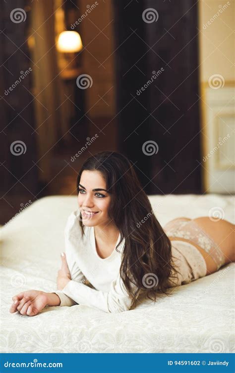 Сексуальная молодая женщина в женское бельё представляя на кровати Стоковое Фото изображение