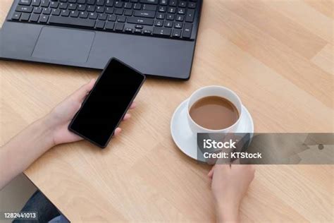 노트북 위에 빈 화면으로 휴대 전화를 들고 나무 책상에 커피 라떼 머그잔을 들고 있는 여성 손 공란에 대한 스톡 사진 및 기타 이미지 Istock