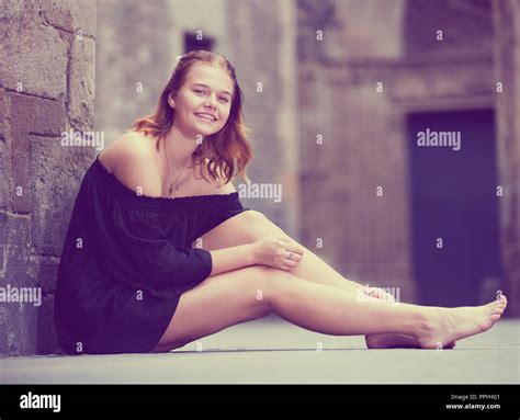 Cheerful Girl Sitting Barefoot Near The Brick Wall In Dress Outdoors