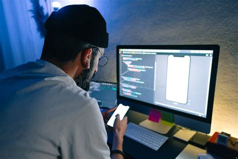 Young Man Mobile Developer Writes Program Code On A Computer And Check App In Smartphone