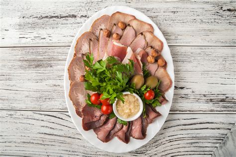 육류와 소시지와 견과류 접시에 슬라이스 마늘 소스 훈제 고기 구운 햄 쵸 릿 죠 베이컨 올리브 체리 토마토 흰색 질감된 나무 테이블의 배경에 대 한 접시에 고기에 대한 스톡