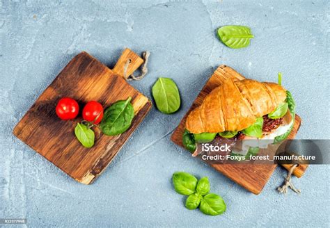 훈제 고기 햄 디 파 르 마와 크루아상 샌드위치 태양 건조 토마토 신선한 시금치와 돌 질감 회색 배경에 작은 소박한 나무 보드에