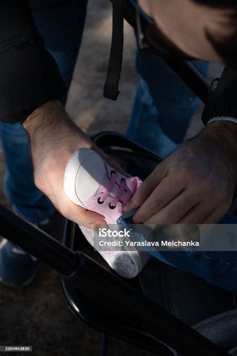 꽃무늬 패턴으로 어린이의 분홍색 신발을 묶는 어른의 클로즈업으로 은은한 조명 아래 야외 환경에서 보살핌과 관심의 부드러운 순간을 강조합니다 활동 유대감 따뜻함 집중 2명에