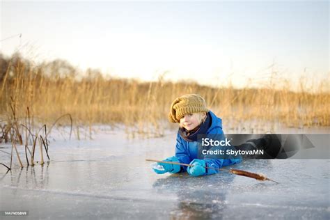 귀여운 미취학 아동이 춥고 화창한 겨울 일몰에 얼어붙은 호수나 강의 얼음 위에서 놀고 있습니다 가족 하이킹 중에 고드름과 마른 갈대 식물로 즐거운 시간을 보내는 아이 어린이