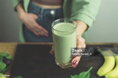 평상복 차림의 알아볼 수 없는 여성이 신선한 건강한 녹색 비건 스무디 한 잔을 들고 있습니다 바나나 시금치 사과 아보카도를 식탁에 올려 놓는다 먹기에 대한 스톡 사진 및