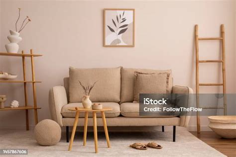 모의 포스터 프레임 우아한 베이지색 소파 나무 원형 커피 테이블 거울 밝은 깔개 사다리 말린 꽃과 개인 액세서리가 있는 흰색 꽃병이 있는 거실 인테리어의 창의적인 구성 가정