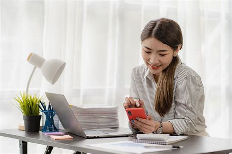 사무실 테이블에 재무 그래프를 분석하기 위해 노트북으로 작업하는 스마트 폰을 들고있는 매력적인 젊은 아시아 비즈니스 여성 경영자에 대한 스톡 사진 및 기타 이미지 Istock