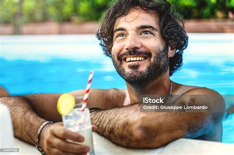 수영장에서 목욕을하면서 상쾌한 칵테일을 마시고 친구들과 채팅하면서 휴식을 취하는 털이 많은 남자의 초상화 여름 방학의 개념과 야외에서 평온한 삶의 개념 남자에 대한 스톡
