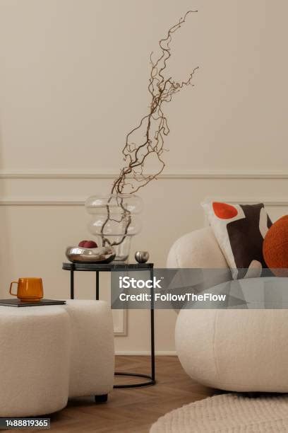 둥근 커피 테이블 나뭇가지가 있는 유리 꽃병 흰색 푸프 모듈식 소파 은색 그릇 무늬가 있는 베개 및 개인 액세서리가 있는 거실 인테리어의 미니멀한 구성 가정 장식 템플렛