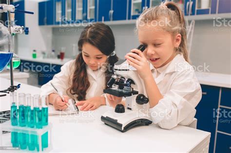 실험실 코트에서 두 작은 아이 학교 실험실에서 화학 학습 실험실 또는 화학 내각에 있는 실험을 만드는 방어적 인 유리에 있는 젊은 과학자 현미경을 통해 보고 Stem 주제에