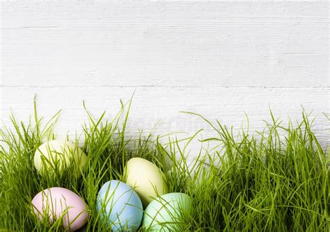 Easter Eggs Laying In Green Grass Near The Old White Wooden Wall