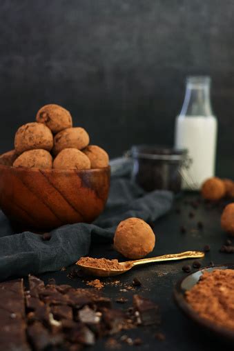 가나슈 센터가 있는 수제 개별 초콜릿 트러플 과자 회색 티타월 금속 숟가락 우유 병 짙은 회색 배경 전경에 초점을 맞춘 나무 그릇에 코코아 파우더를 더럽힌 고급 초콜릿 볼