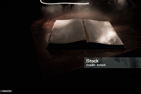 반짝이는 황금색 배경이 있는 나무 탁자 위에 열린 고대 책의 그림책을 상상해 보십시오 마법의 힘으로 마법 빛나는 책 주위 번개 어둠의 방에서 0명에 대한 스톡 사진 및 기타