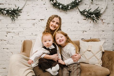 메리 크리스마스와 해피 홀리데이 집에서 젊은 가족 사진입니다 엄마는 아들과 딸이 함께 시간을 즐기고 있다고 포옹합니다 어머니는 아이들을 껴안습니다 집의 인테리어를 장식 근접