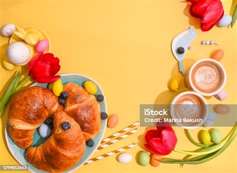 크루아상과 베리가 함께 한 봄 아침 식사 밝은 컵에 에스프레소 커피 두 개 부활절 초콜릿 달걀 분홍색 토끼 귀와 노란색 배경에 빨간 튤립 공간을 복사합니다 플랫 레이 0명에
