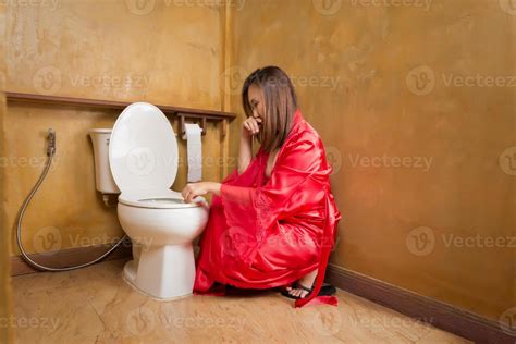Asian Woman In A Nightgown And Red Satin Robe Wiping The Toilet Seat At Night Stock