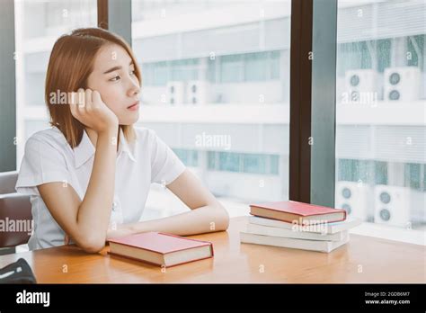 Asian university girl teen sitting alone thinking worry, day dreaming or boring looking out ...