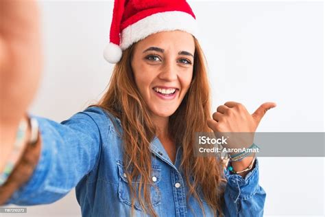크리스마스 모자를 쓰고 셀카를 찍고 행복한 얼굴미소를 지으며 엄지 손가락으로 보여주는 젊은 아름다운 빨간 머리 여성 가리키기에 대한 스톡 사진 및 기타 이미지 Istock