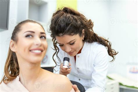 Female Dermatologist Carefully Examining The Skin Of A Female Patient Using A Dermascope