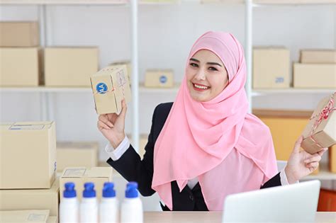 파란색 무슬림 정장을 입은 활동적인 아시아 여성이 앉아서 컴퓨터로 일하고 행복한 웃는 얼굴로 온라인 소포 상자 배달을 보여주고 있다 스타트업 중소기업 프리랜서 일하는 소녀가