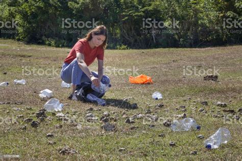 초원에서 플라스틱 병을 집어 들고있는 여자 플라스틱 쓰레기를 수거하는 환경 운동가의 사진 자원 봉사자는 야외에서 사용되는
